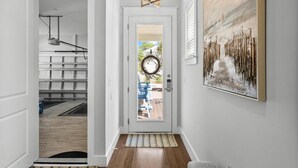 Um corredor com porta branca, chão de madeira, luminária pendente e um quadro na parede.