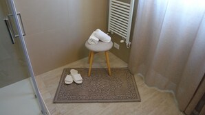 Um banheiro com chuveiro, uma toalha em um banquinho e chinelos no chão.