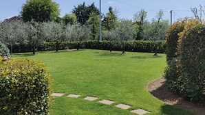 Um gramado bem cuidado com pedras para pisar, cercado por sebes e árvores bem aparadas.