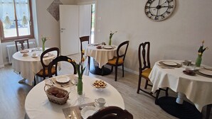 Uma sala de jantar com mesas redondas, cadeiras e um relógio na parede.