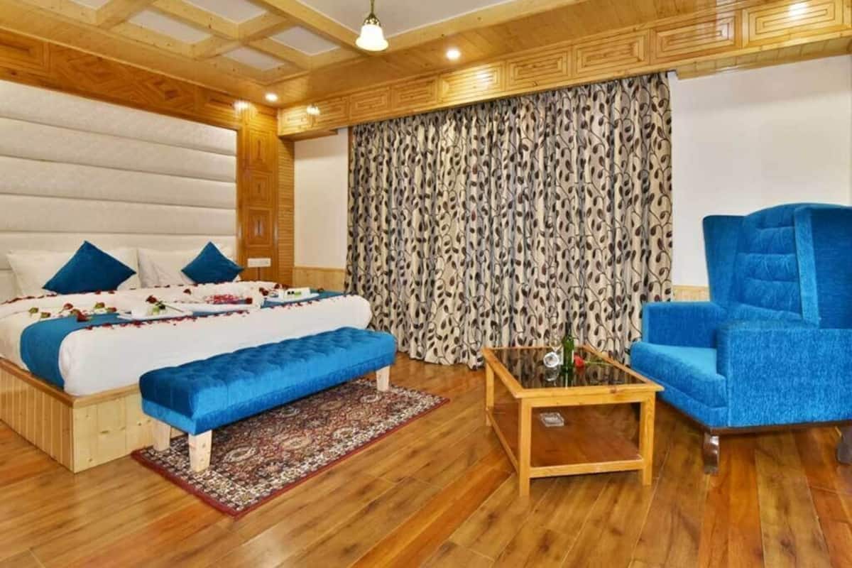 Quarto com cama, sofá azul, mesa de centro e cortinas estampadas.