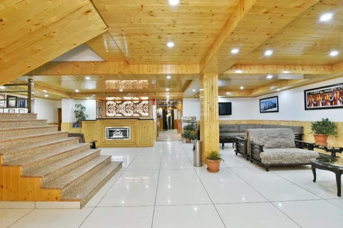 Interior em madeira com balcão de recepção, escada, sofá e plantas em vasos.