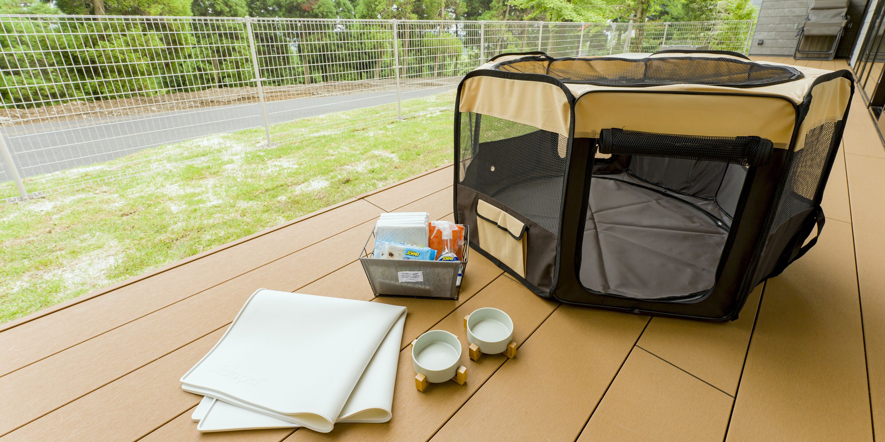 Uma cama para animais de estimação em um deck de madeira, com vista para uma área cercada e vegetação.
