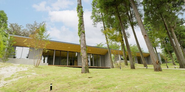 Um edifício moderno com grandes janelas de vidro, rodeado por árvores e um gramado.