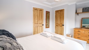 Quarto com uma cama grande, portas de madeira, cômoda e luminária pendente.