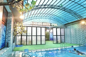 Piscina interna com teto de vidro, placa indicando "BINH AN NHIEN POOL" e cadeira do salva-vidas.