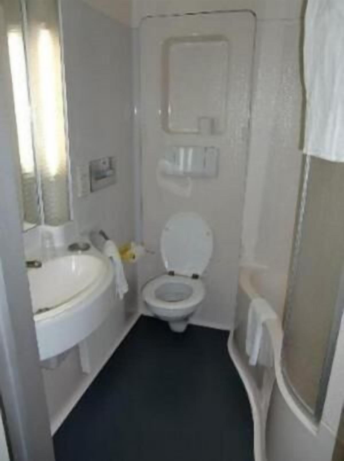 Casa de banho pequena e compacta, com lavatório, sanita e zona de duche brancos.