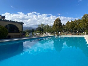 Piscina com cadeiras de sol e vista para montanhas ao fundo.