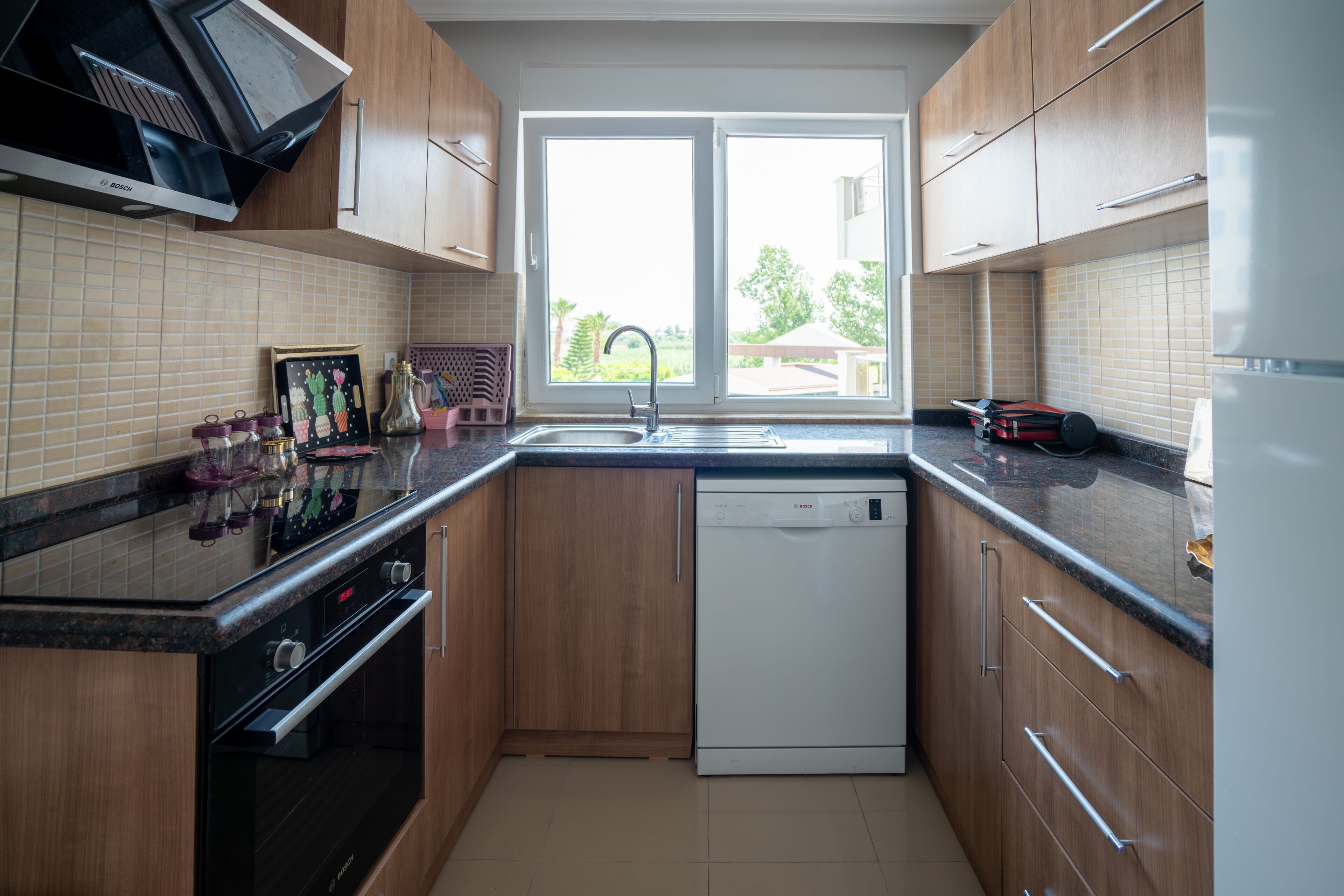 Cozinha moderna com armários de madeira, máquina de lavar louça Bosch e janela que proporciona luz natural.