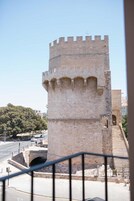Uma torre de pedra histórica com uma escadaria que leva até ela, localizada perto de uma estrada moderna e árvores.