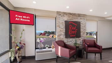 Um saguão de hotel com um letreiro indicando 'Wi-Fi Gratuito em Todos os Quartos', um letreiro da 'Red Roof Inn' e duas poltronas vermelhas.