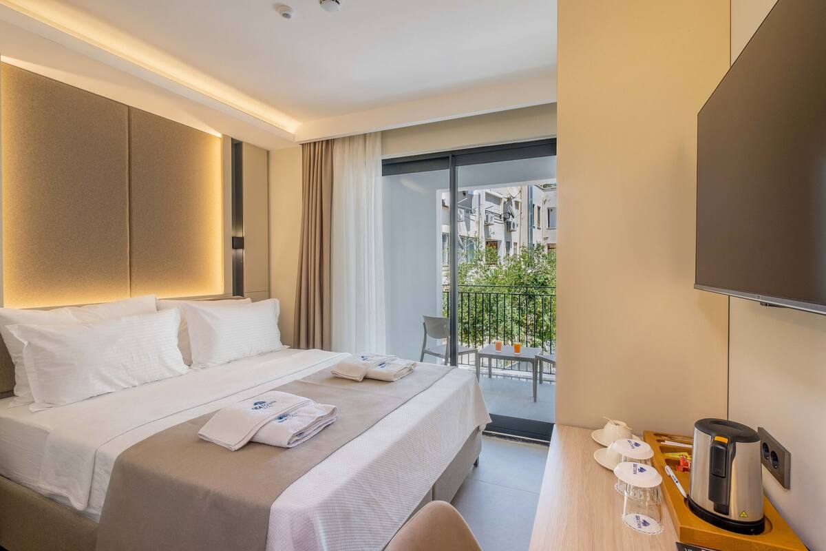 Quarto de hotel com cama, secretária com máquina de café e vista da cidade através de uma varanda.
