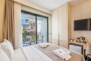 Quarto de hotel com cama, escrivaninha com cafeteira, televisão e varanda com vista para a cidade.