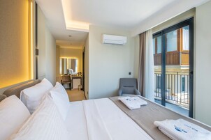 Quarto de hotel com uma cama grande, uma escrivaninha com cadeira, ar condicionado e varanda com vista.