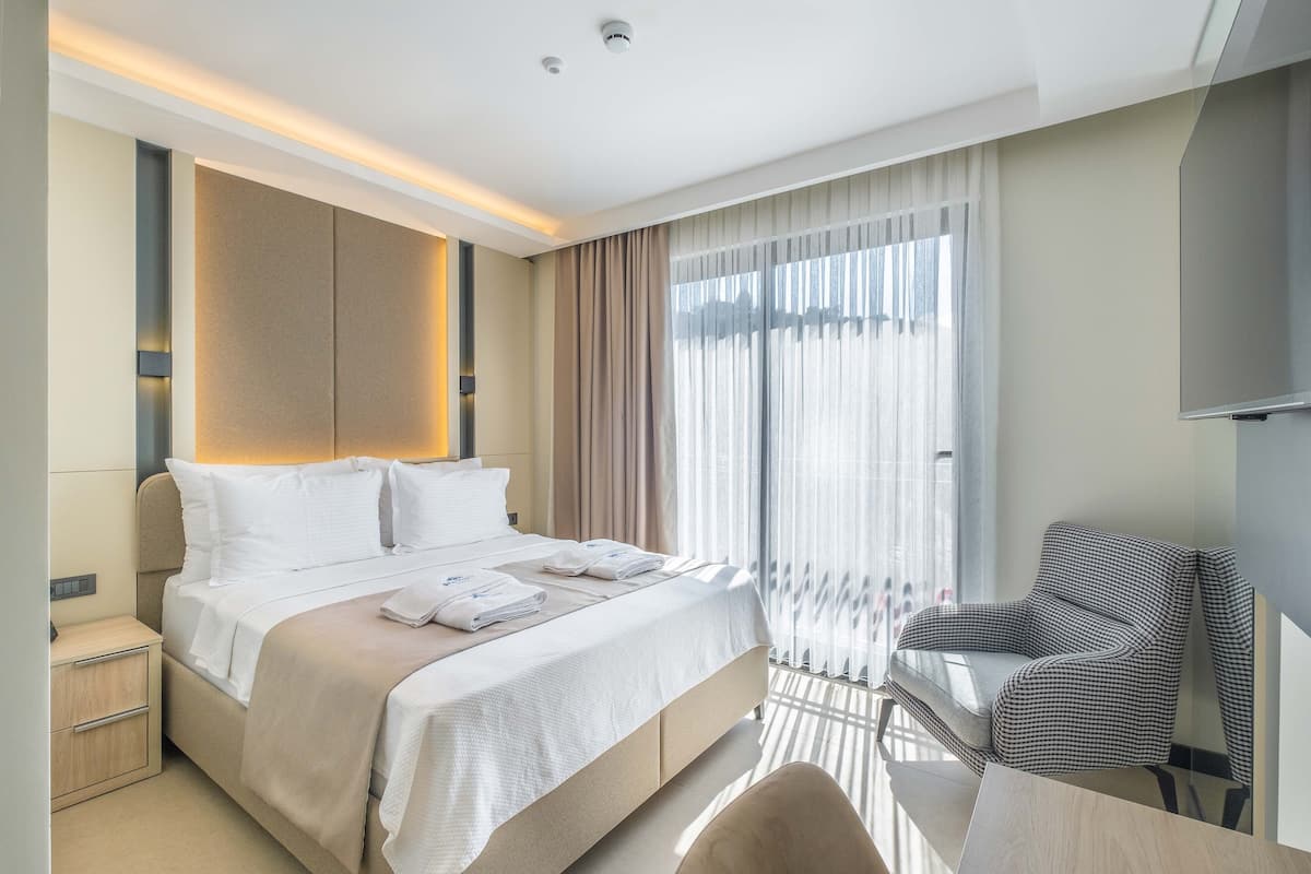 Quarto de hotel moderno com uma cama grande, uma escrivaninha, uma cadeira e uma televisão.