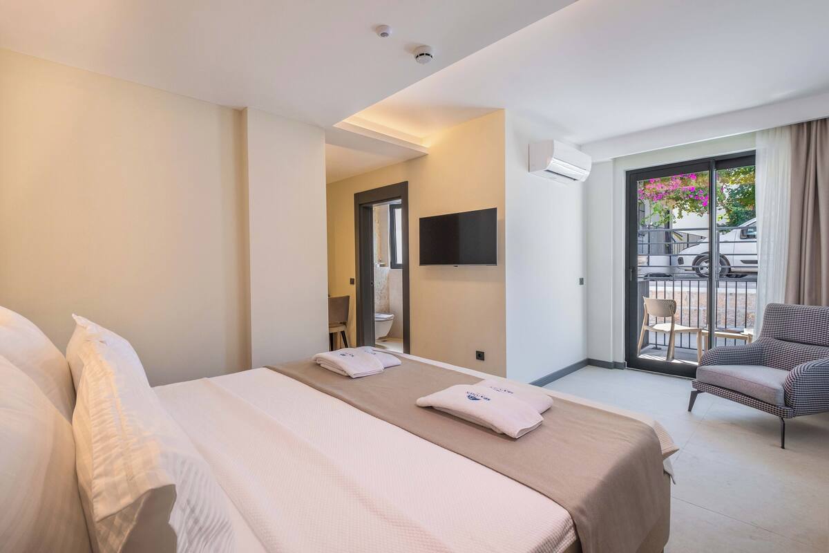 Quarto de hotel com cama, poltrona, televisão e varanda com vista exterior.