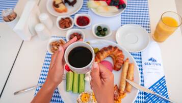 Prato de café da manhã com ovos, bacon e um croissant, uma xícara de café e um copo de suco de laranja sobre uma toalha xadrez.