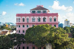 Um edifício rosa com janelas em arco e telhado telhado, rodeado por árvores e outros edifícios.