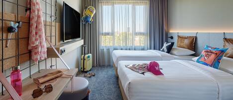 Quarto de hotel com duas camas, televisão, um mural com objetos e uma janela com cortinas.