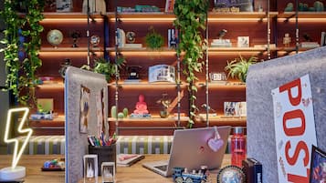 Um espaço de trabalho acolhedor com um laptop, uma pequena luminária de mesa e uma estante repleta de livros e objetos decorativos.