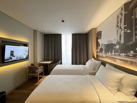 Quarto de hotel com duas camas, uma TV fixada na parede, uma mesa pequena e uma cadeira.
