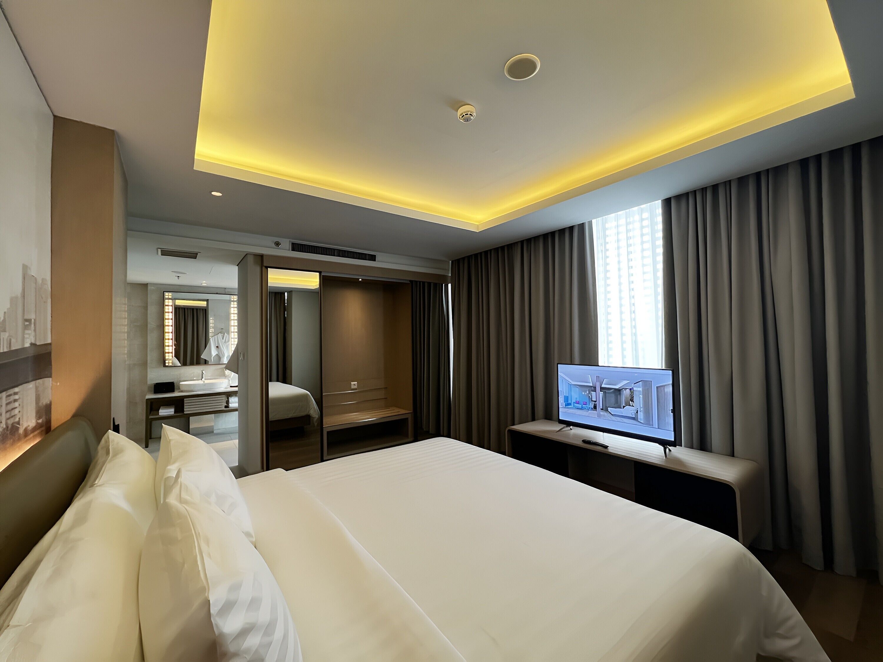 Quarto de hotel moderno com uma cama grande, uma escrivaninha com computador, televisão e banheiro com espelho.