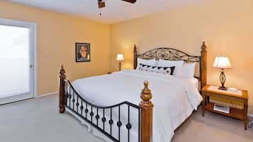 Quarto com cama, mesa de cabeceira, ventoinha no teto e porta.