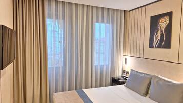 Quarto de hotel com uma cama grande, mesa de cabeceira, televisão e um quadro na parede.
