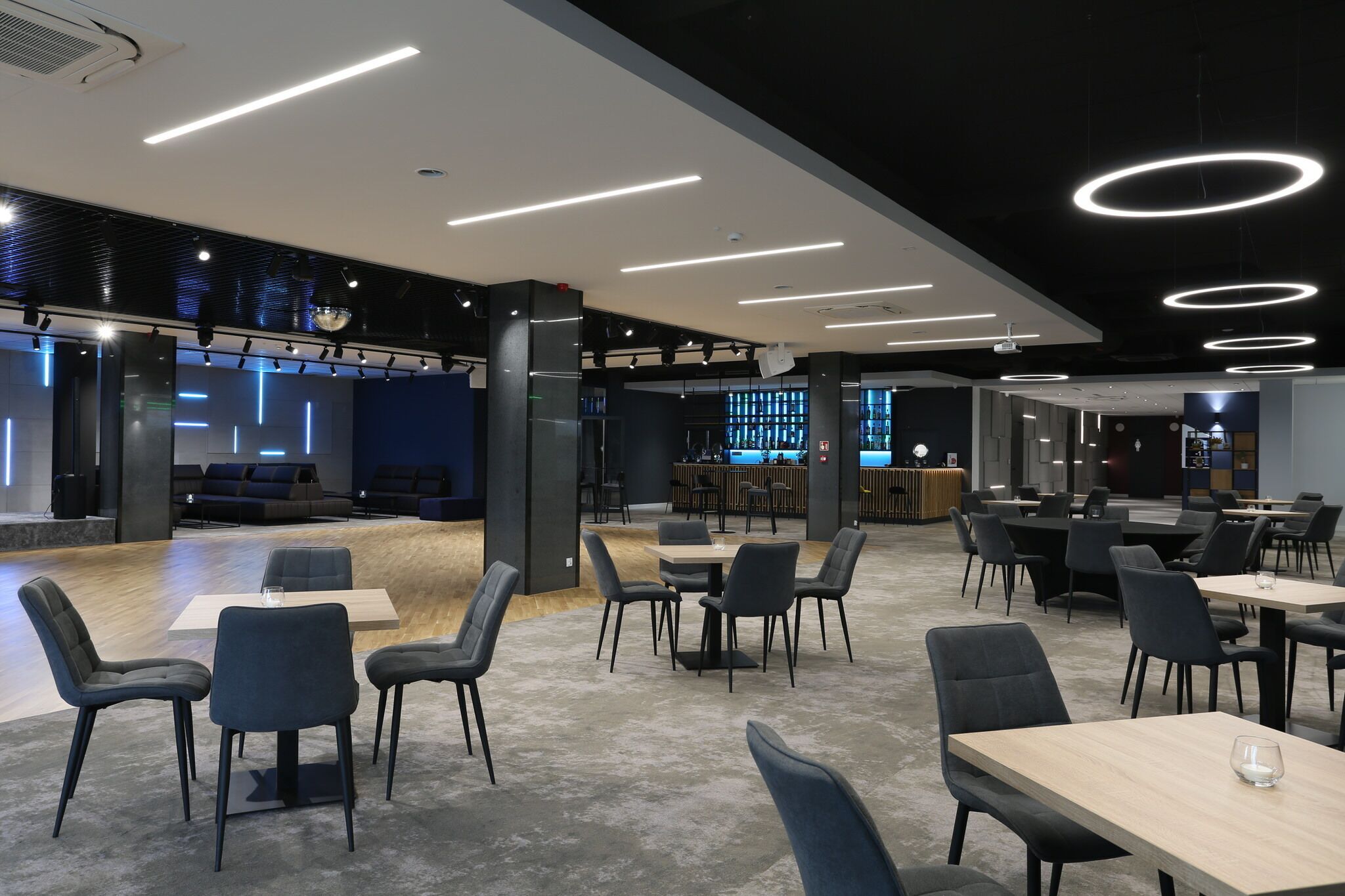 Espaço interior moderno com áreas de estar, mesas e um bar.