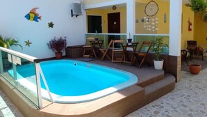 Piscina com barreira de vidro, deck de madeira e vasos de plantas.