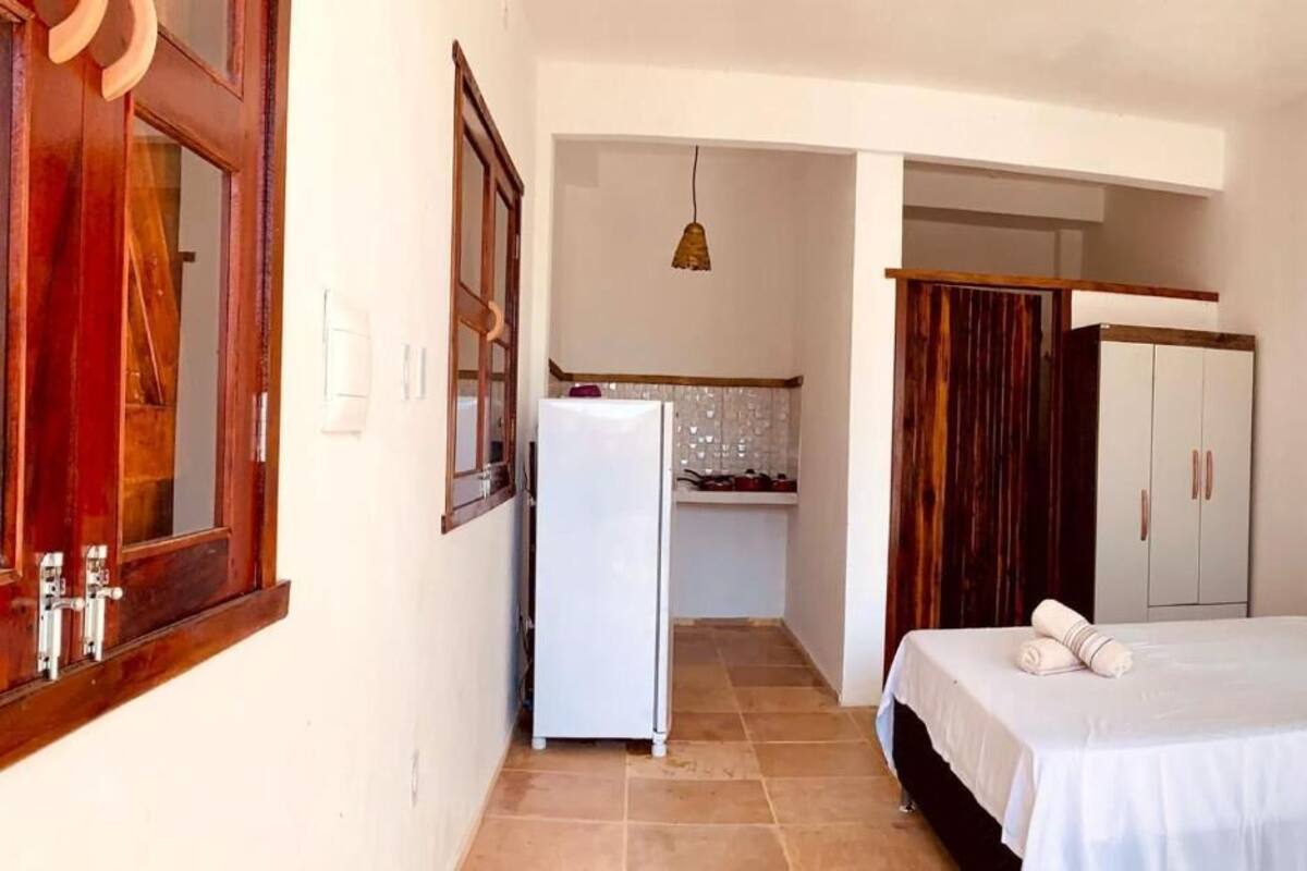 Quarto com cama, guarda-roupa, pequena cozinha e porta que dá para outro espaço.