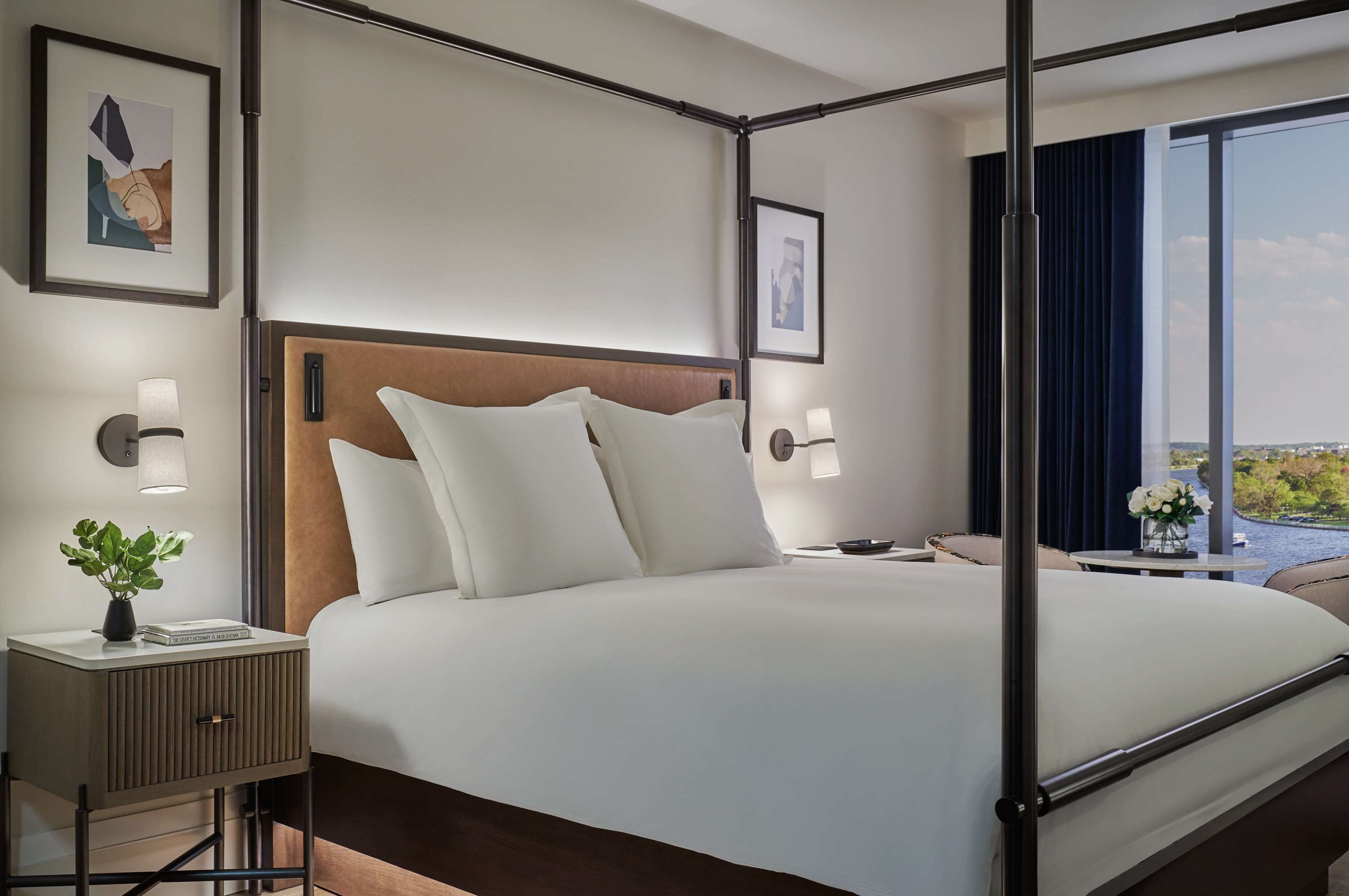 Quarto de hotel moderno com uma cama grande, mesas de cabeceira com abajures e obras de arte nas paredes.