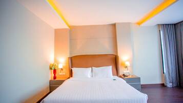 Quarto de hotel com uma cama grande, duas mesas de cabeceira com luminárias, um criado-mudo e um vaso com flores.
