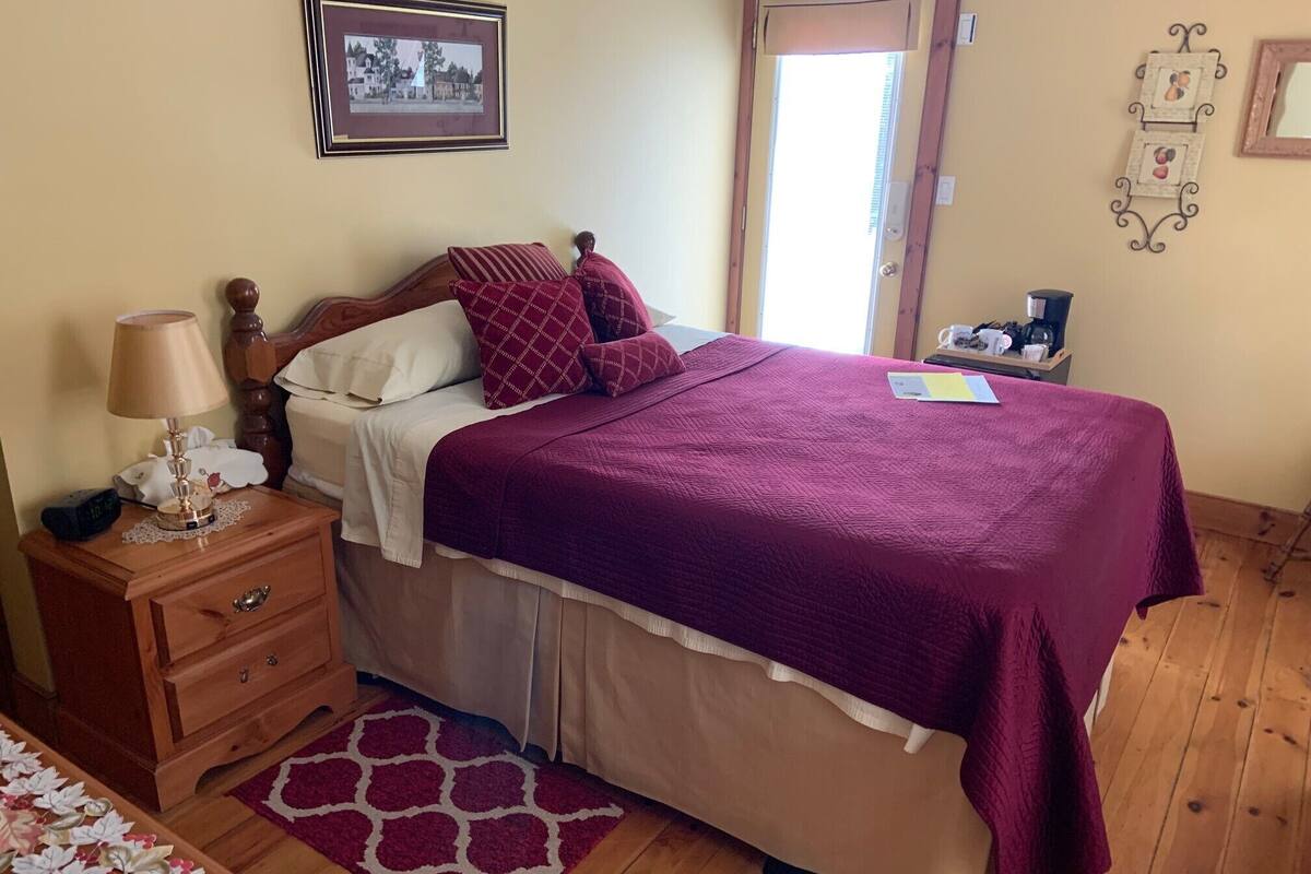 Quarto com cama, mesa de cabeceira, abajur, quadro emoldurado e porta.