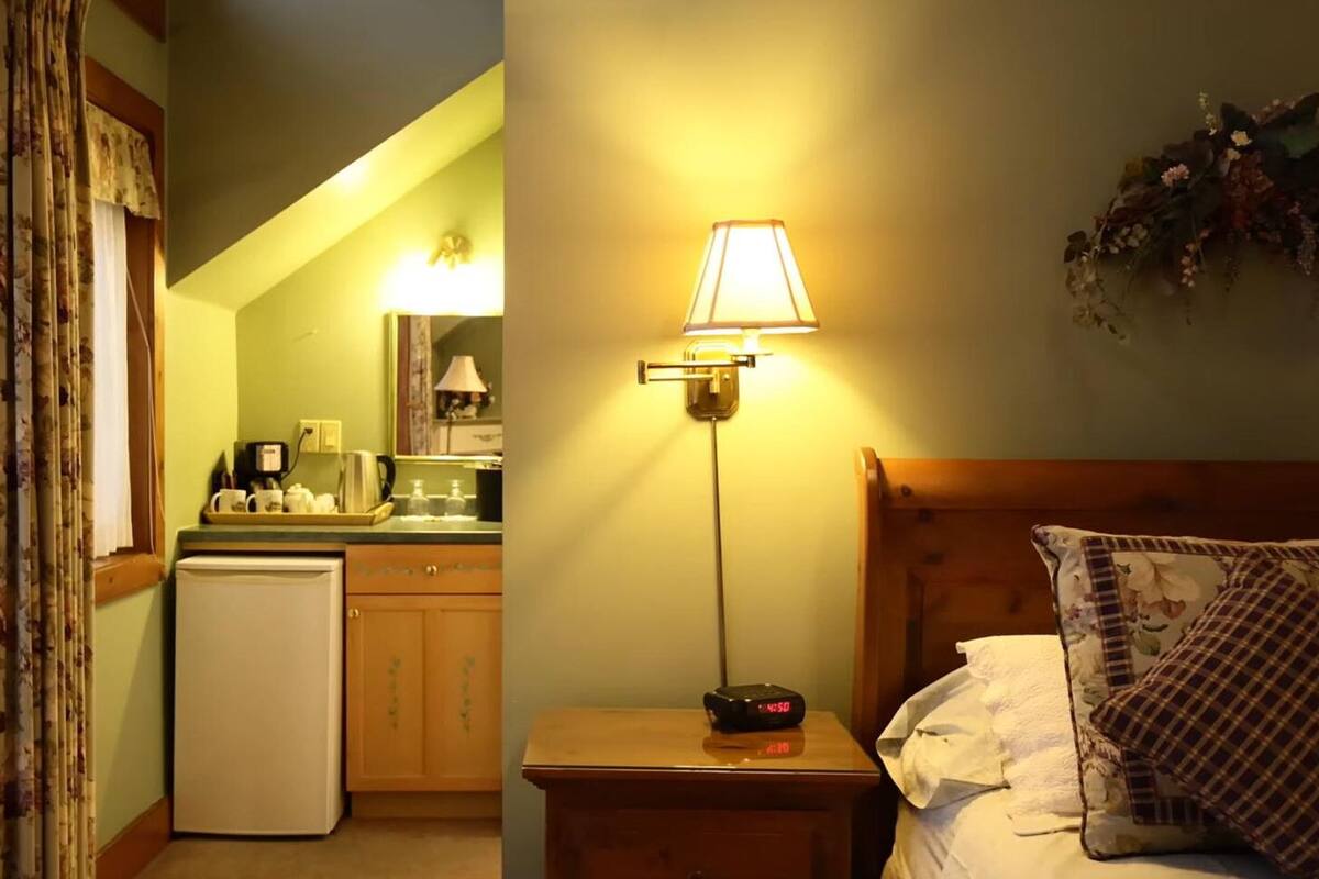 Quarto de hotel compacto com cozinha compacta, luminária ao lado da cama e decoração floral na parede.