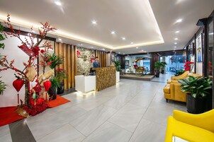 Uma área de recepção de hotel com balcão de mármore, detalhes decorativos vermelhos e assentos amarelos.