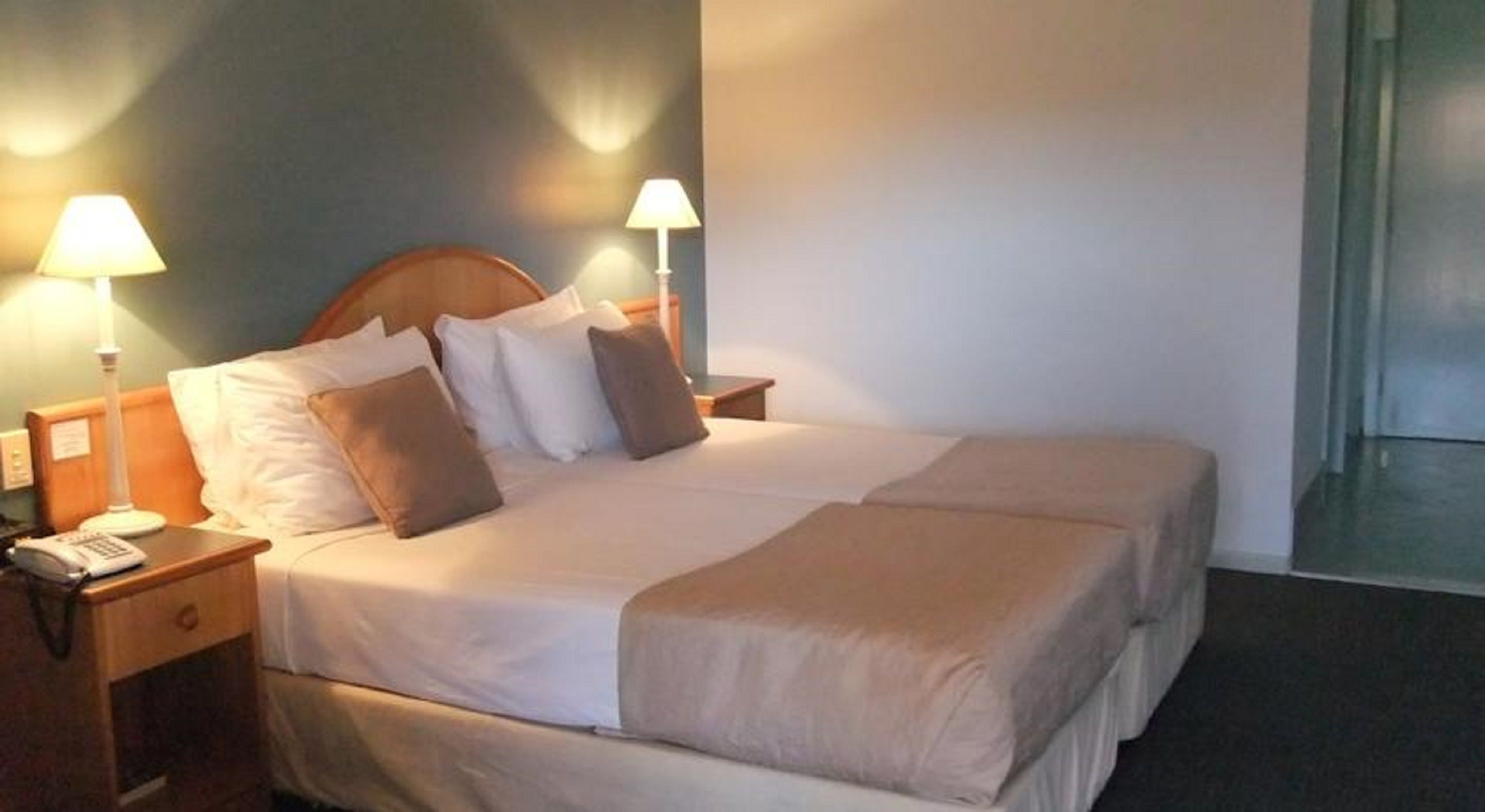 Quarto de hotel com duas camas, uma mesa de cabeceira com abajur e um telefone.