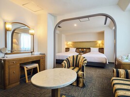 Quarto de hotel com escrivaninha, duas camas, uma mesa redonda e um espelho.