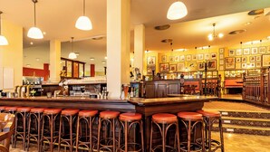 Uma área de bar com banquetas de madeira, balcão e parede decorada com quadros.