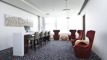 Sala de conferências moderna com mesa branca, várias cadeiras, carpete estampado e arte abstrata nas paredes.