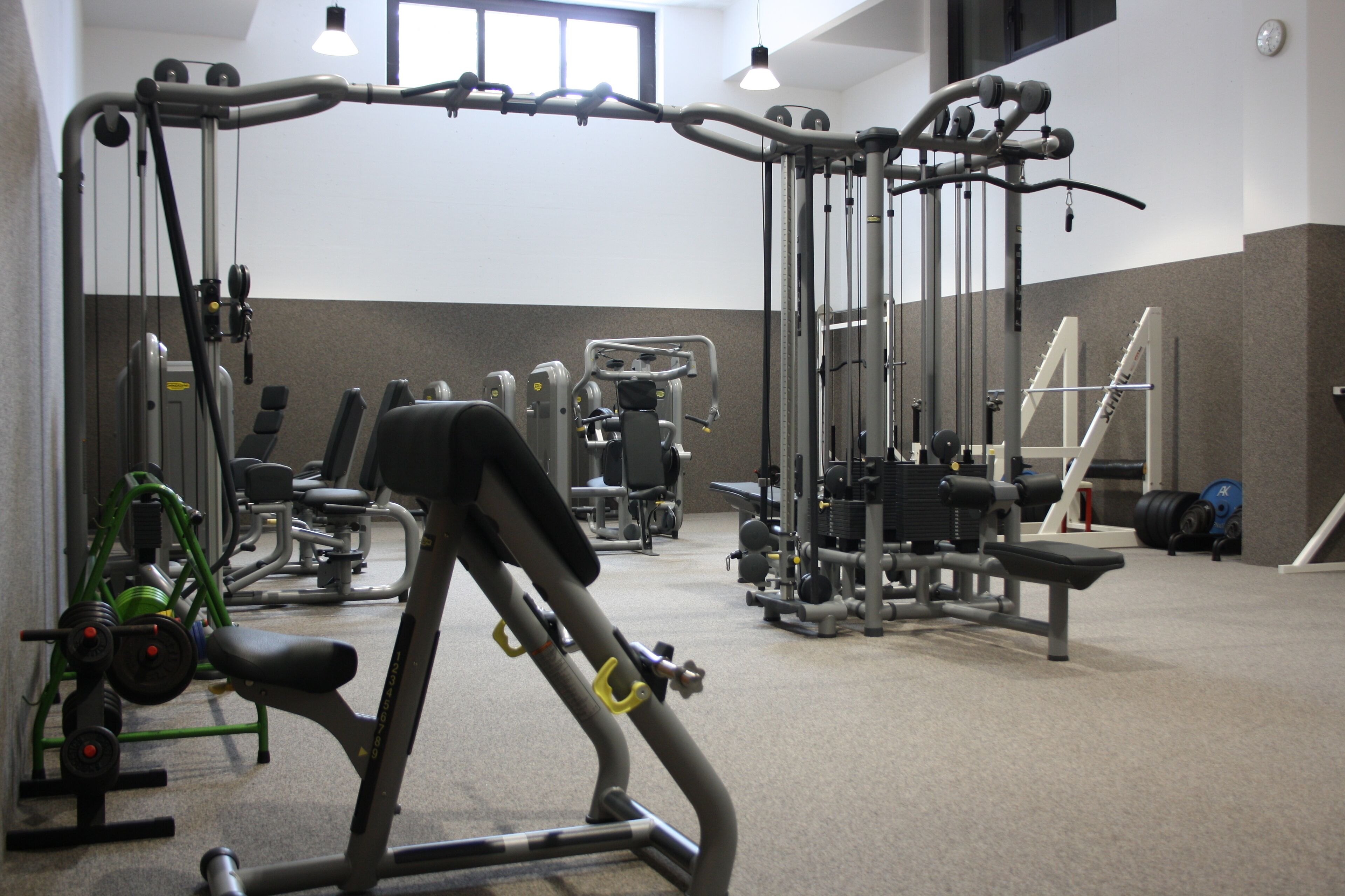 Uma academia com diversos equipamentos de exercícios, incluindo supino, aparelhos de musculação e pesos livres.
