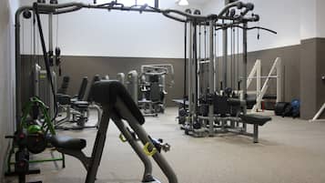 Uma academia com diversos equipamentos de exercícios, incluindo supino, aparelhos de musculação e pesos livres.