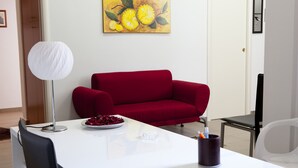 Uma sala de estar moderna com uma mesa branca, um sofá vermelho, um abajur branco e um quadro de limões na parede.