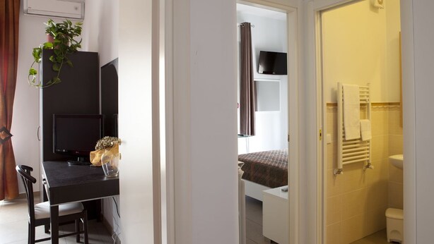 Quarto de hotel compacto com escrivaninha, cadeira e cama com televisão.