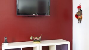 Televisão de tela plana presa a uma parede vermelha, um console branco com um cesto decorativo e uma estátua sobre o console.