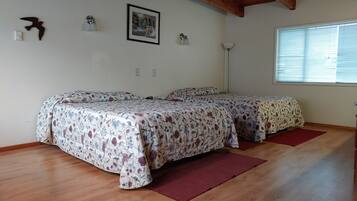 Quarto com duas camas, piso de madeira, tapete vermelho, janela com persianas e teto com vigas aparentes.