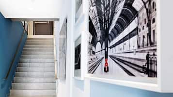 Uma escadaria que leva a uma porta, uma parede com uma fotografia a preto e branco de uma estação de trem, e uma parede azul.