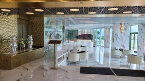 Um lobby moderno de hotel com piso de mármore, balcão de recepção e área de estar com cadeiras brancas.