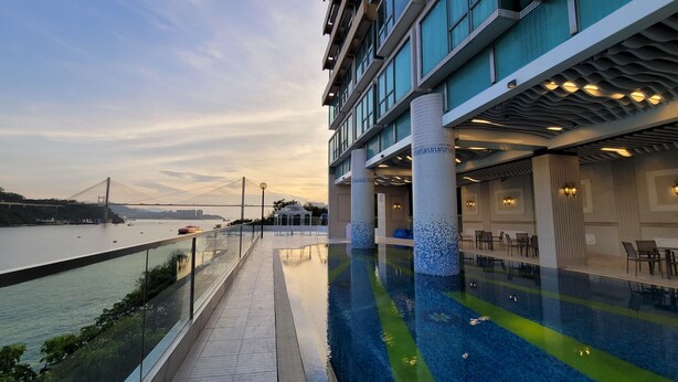 Um hotel moderno com piscina infinita no terraço e vista para um rio e uma ponte.
