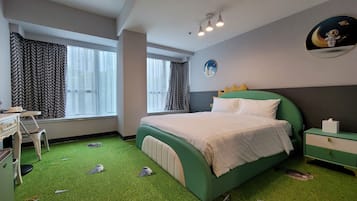 Quarto de hotel com carpete verde, cama com roupa de cama branca, escrivaninha com cadeira e mesa de cabeceira com caixa de lenços.